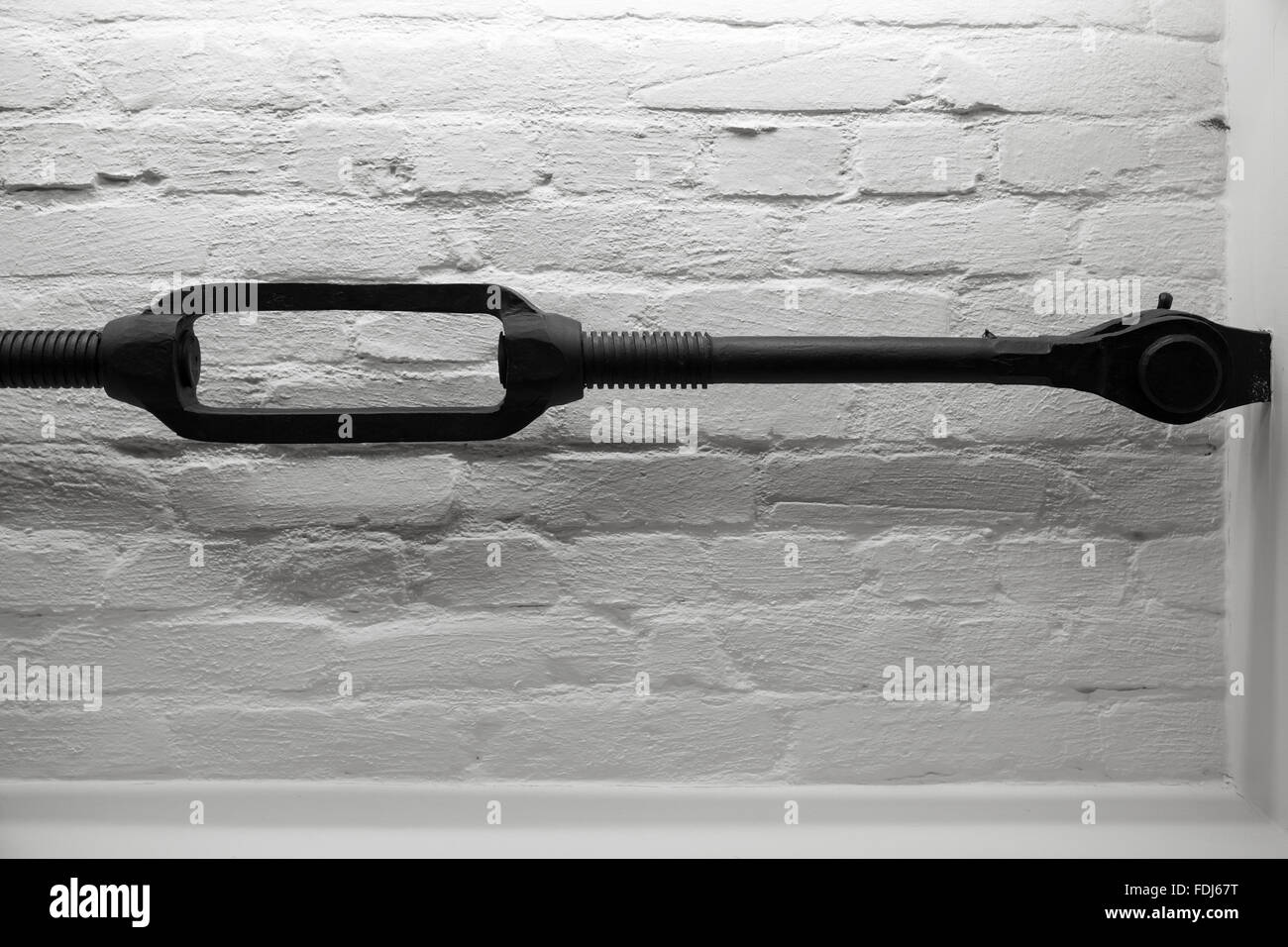 Old black turnbuckle used in building structure over white brick wall ...