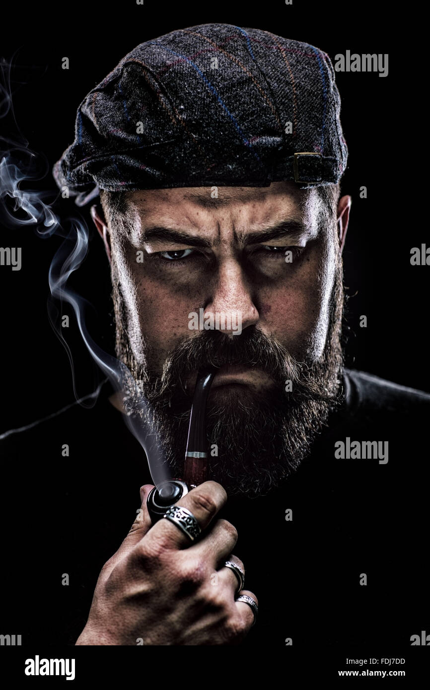 Vertical shot of an angry man with a thick beard smoking a pipe and ...