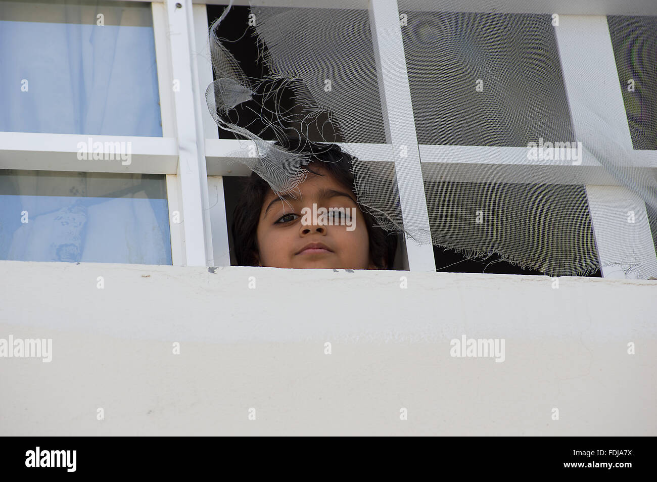 A child in Muscat, Oman looks out of a broken window through a torn ...