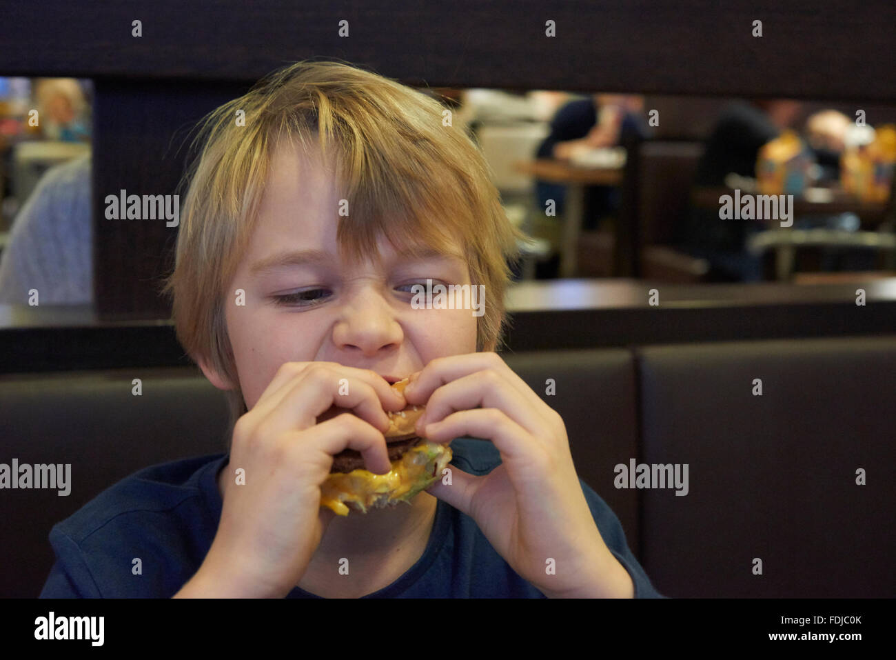 Child blond boy eats hamburger in fastfood Stock Photo - Alamy