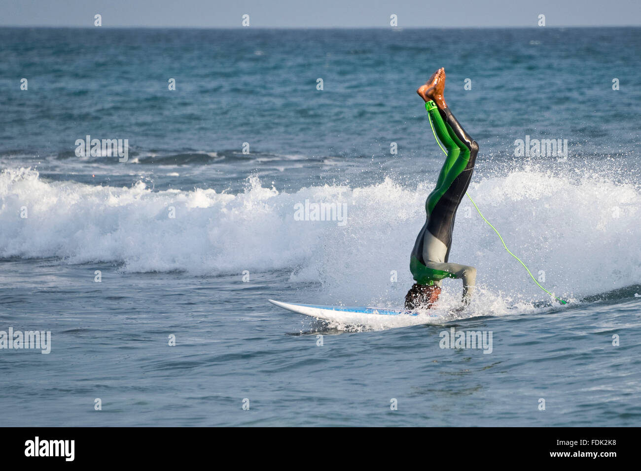 A surfer performing a handstand on his board as the wave breaks in ...