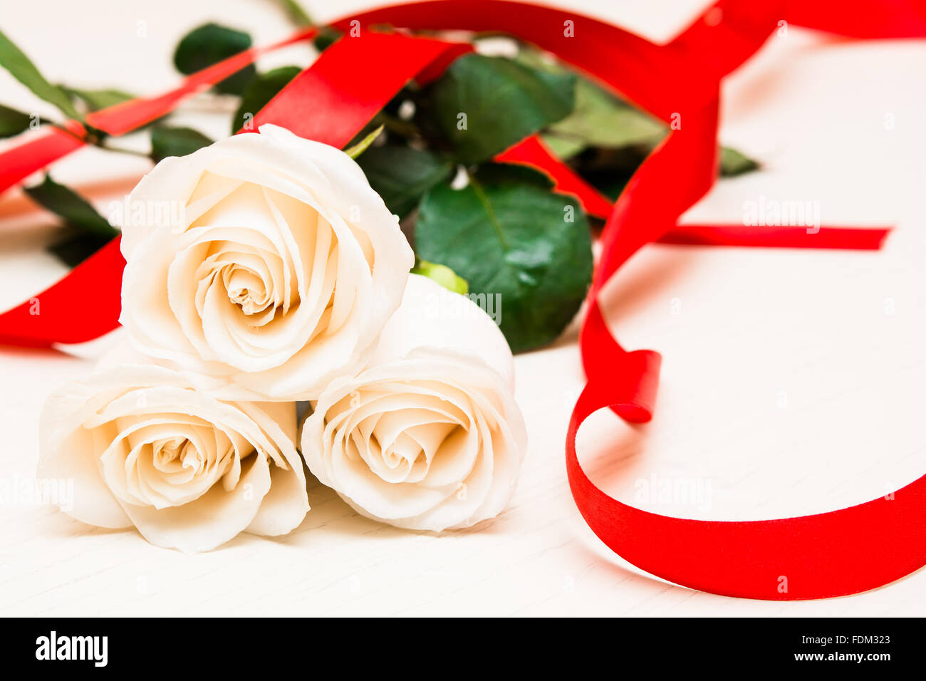 White roses with red ribbon on a light wooden background. Women' s day ...