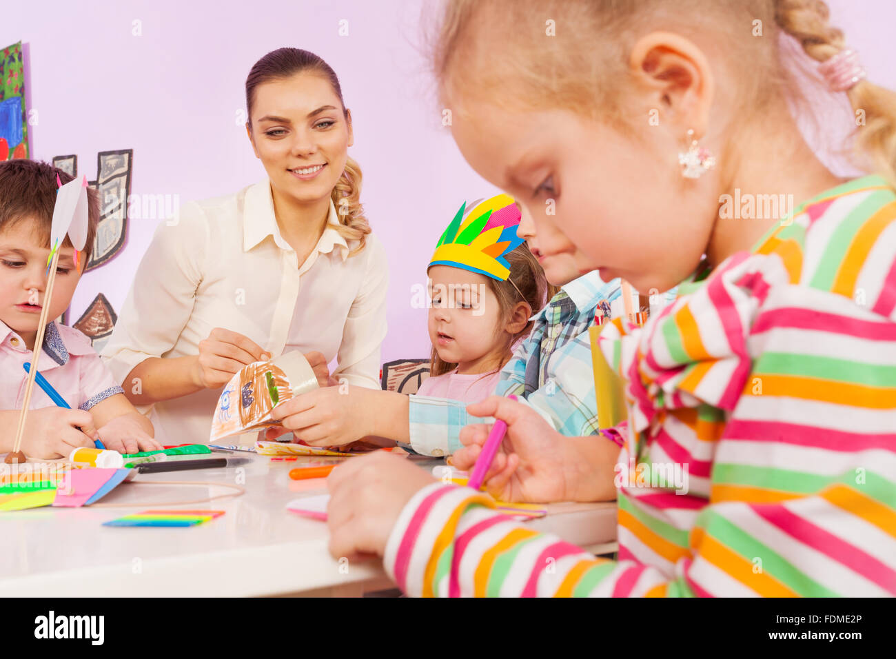 Teacher in kindergarten help kids make paper craft Stock Photo - Alamy