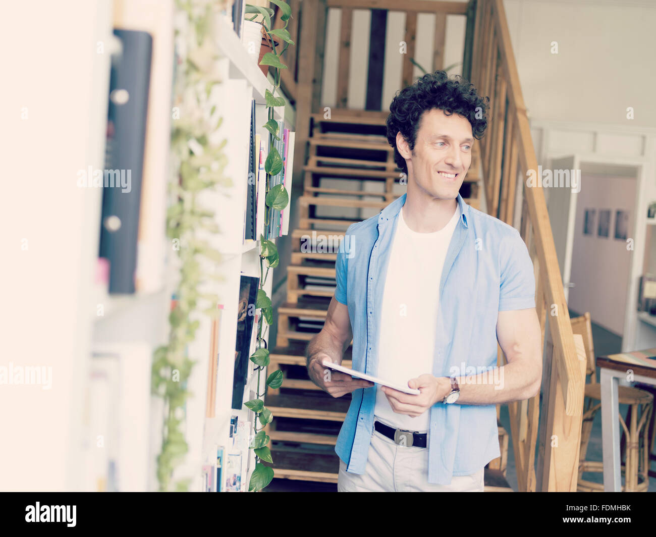 Man with a magazine standing next to bookcase Stock Photo - Alamy