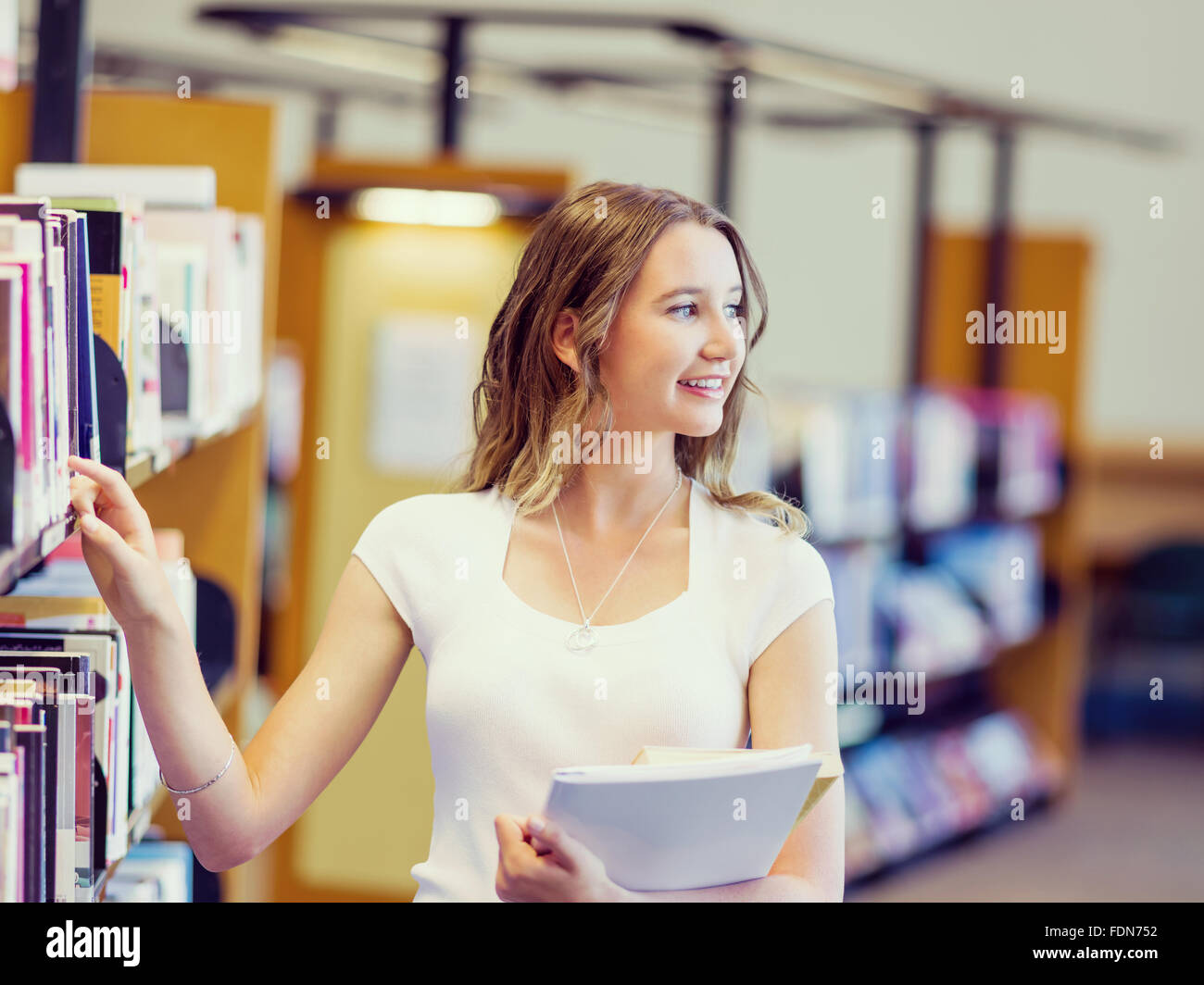 Happy young female student holding books at the library Stock Photo - Alamy