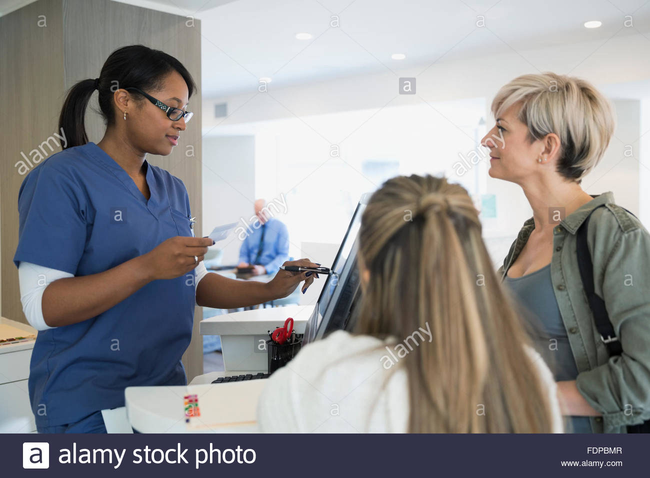 Nurse checking patient in at computer clinic lobby Stock Photo - Alamy