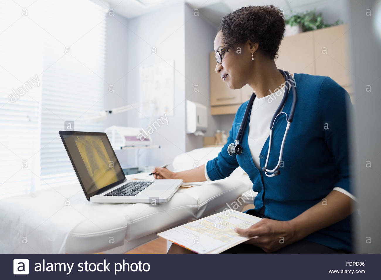 Doctor working at laptop in examination room Stock Photo - Alamy