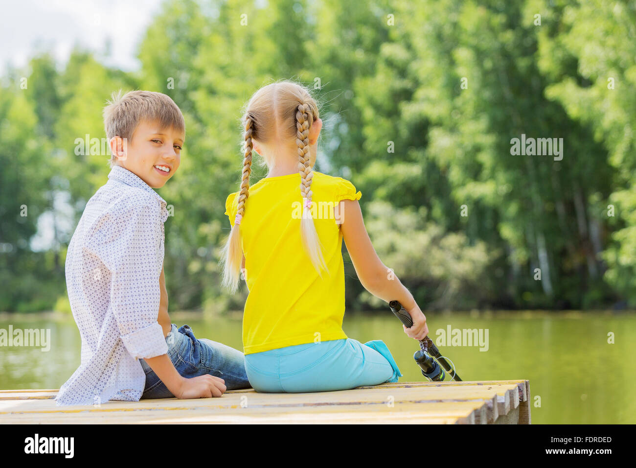 Rear view of two children sitting at bank and fishing Stock Photo - Alamy