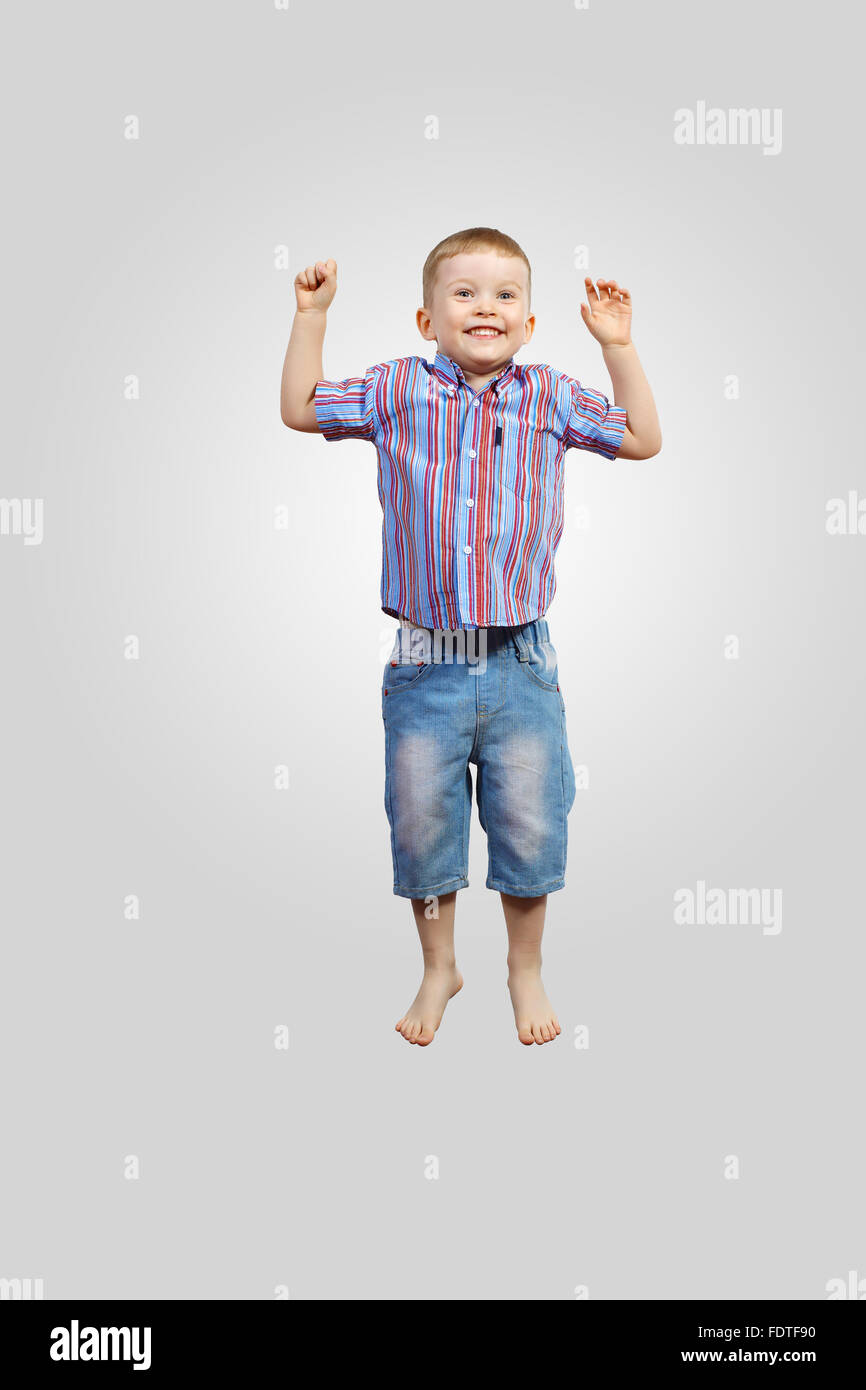Photo of little boy jumping and raising hands against grey background ...