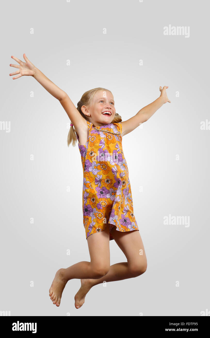 Photo of little girl jumping and raising hands against grey background ...