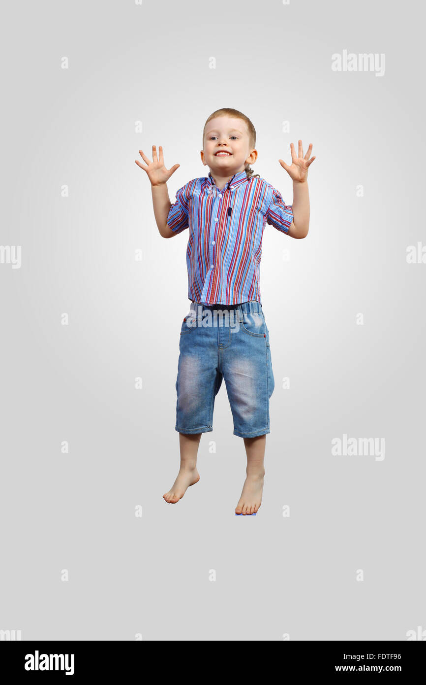 Photo of little boy jumping and raising hands against grey background ...