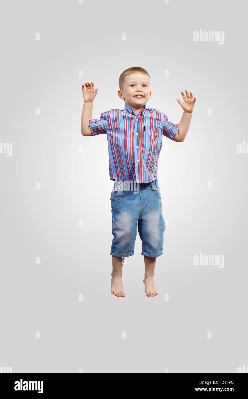 Photo of little boy jumping and raising hands against grey background ...