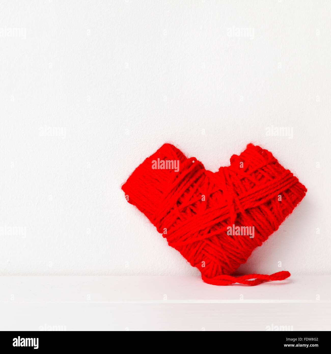 closeup of a heart-shaped coil of red yarn on a white surface against a ...