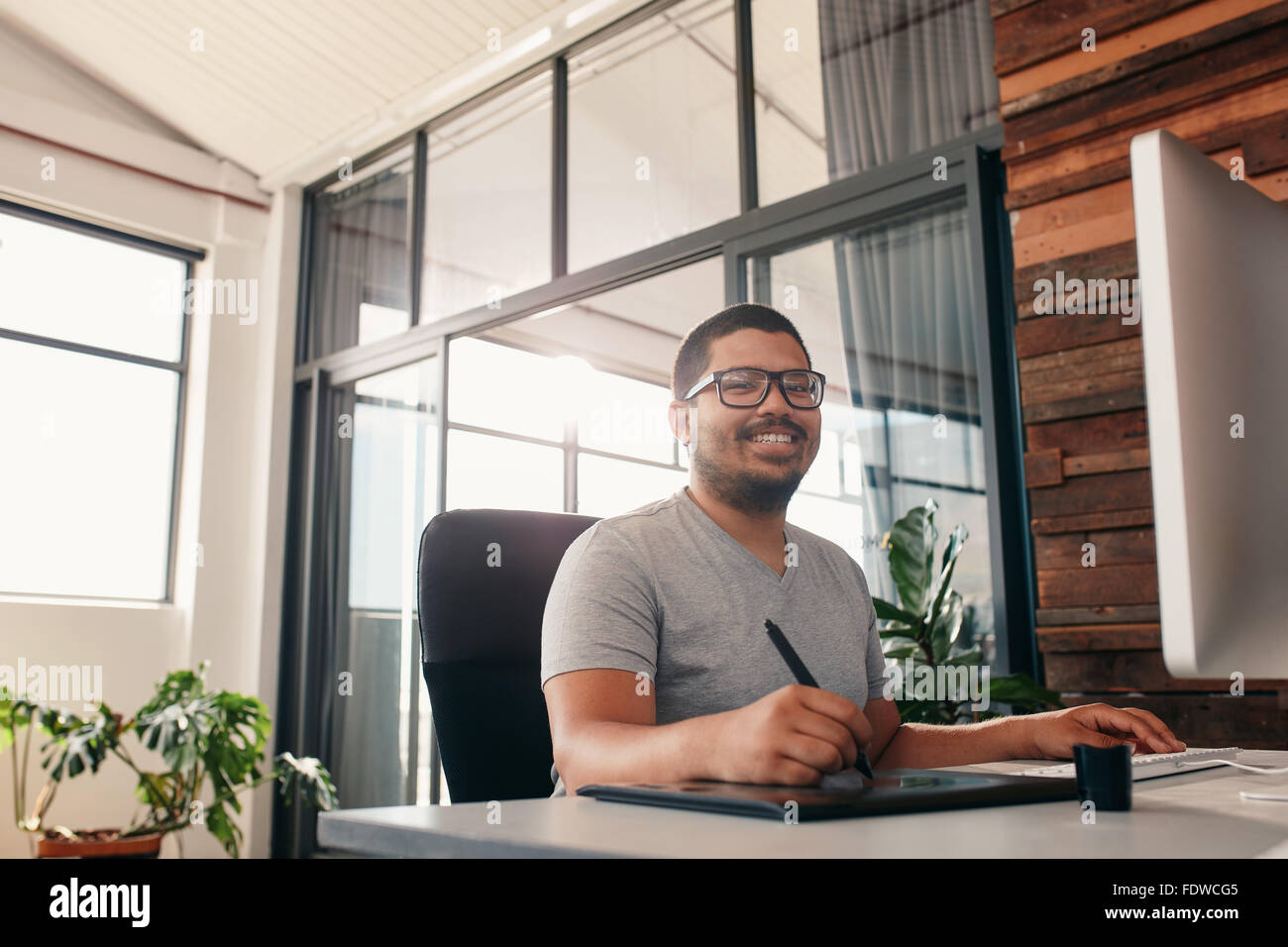 Portrait of cheerful young man sitting at his desk and working with ...