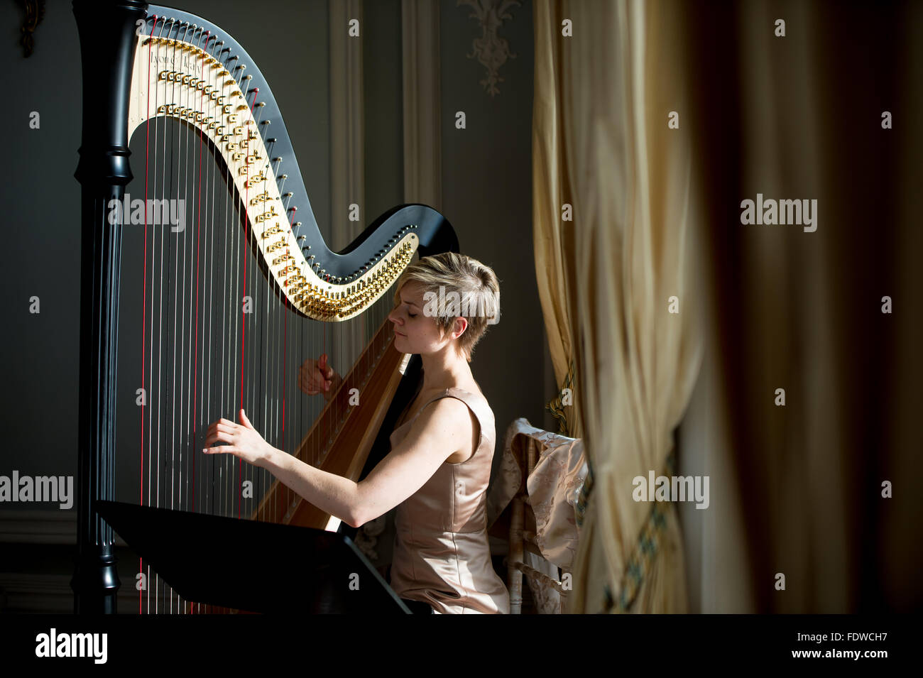 A harpist playing in with the sun shining through the window in an old ...