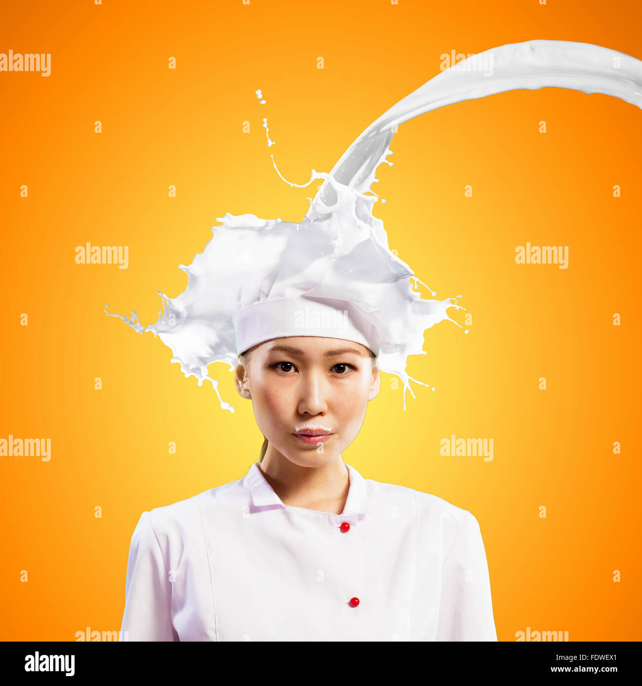 Asian female cook standing against milk splashes in red apron against ...