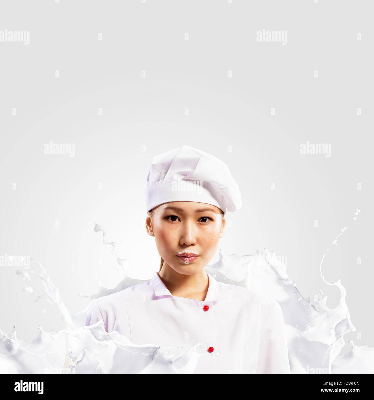 Asian female cook standing against milk splashes in red apron against ...