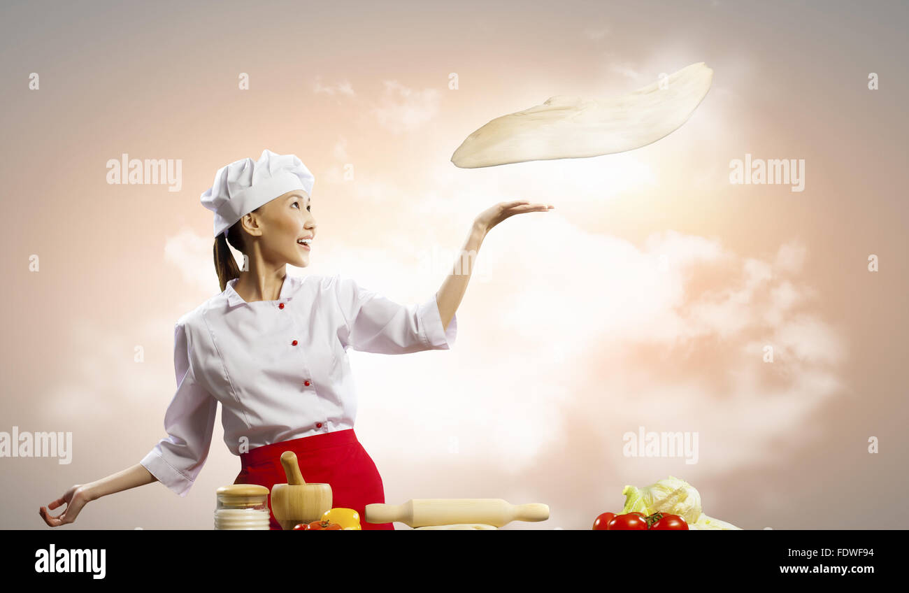 Asian female cook making pizza standing against color background Stock ...
