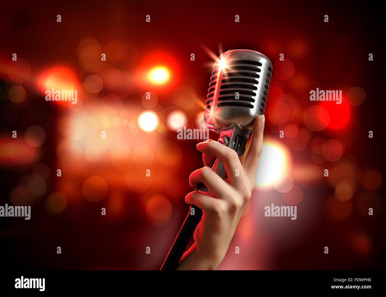 Female hand holding a single retro microphone against colourful ...