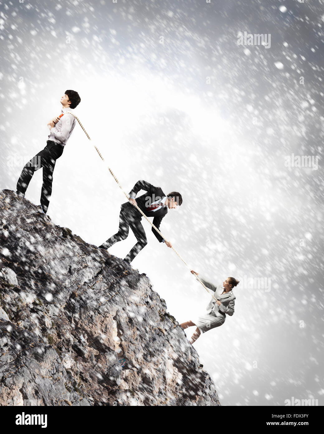 Image of three businesspeople pulling rope atop of mountain under ...