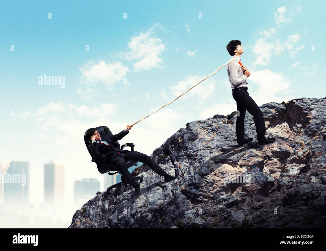 Image of two young businessmen pulling rope atop of mountain against ...