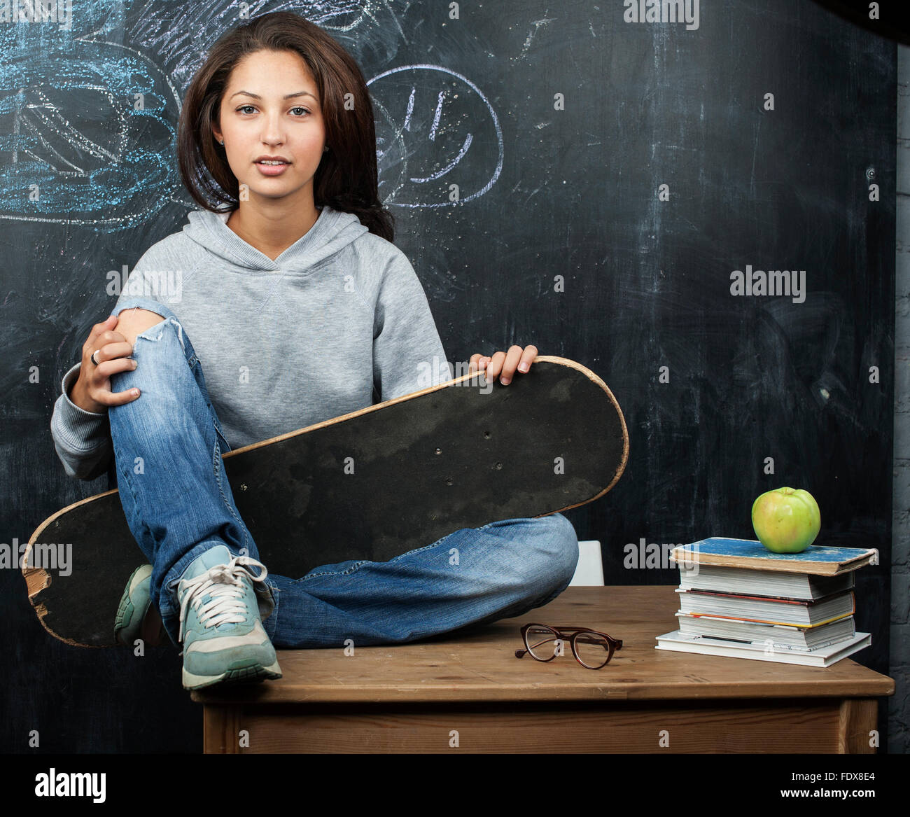 young cute teenage girl in classroom at blackboard seating on table ...