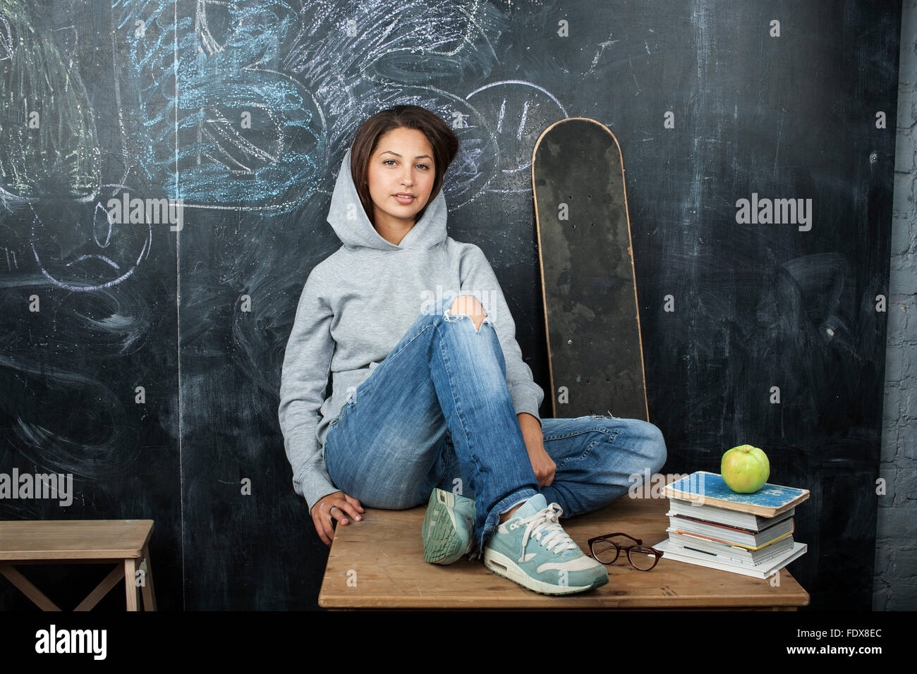 young cute teenage girl in classroom at blackboard seating on table ...