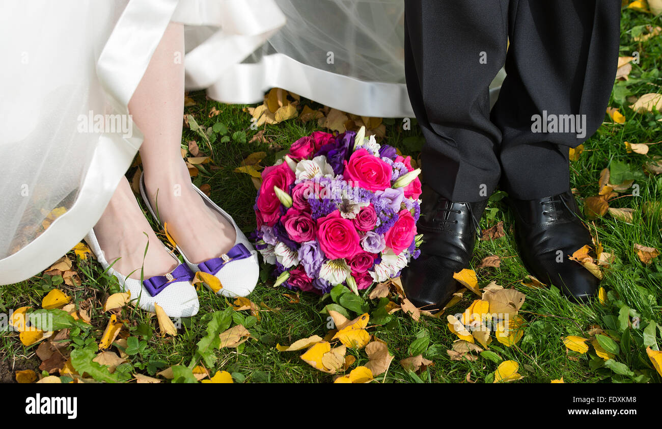 Close-up view of a beautiful wedding bouquet, groom and bridal legs ...