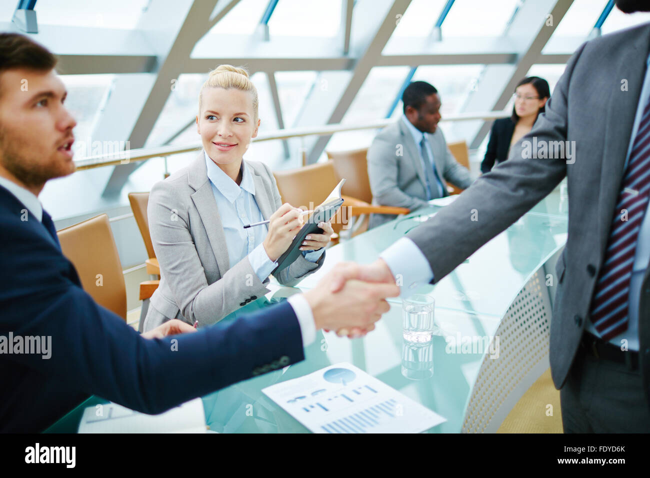 Happy businesswoman looking at one of businessman handshaking with ...