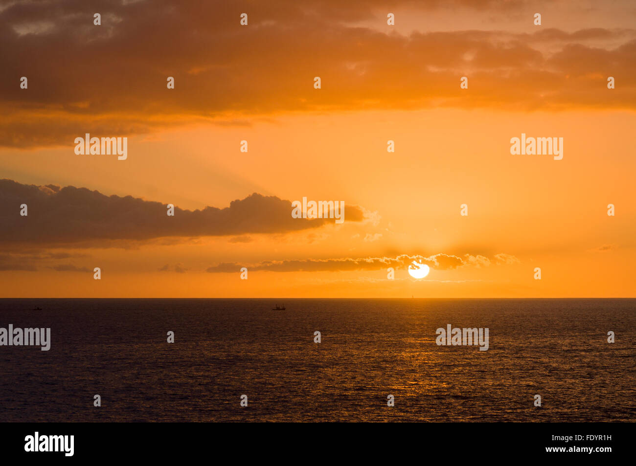 Sunset at ocean, partly hidden sun by clouds Stock Photo - Alamy