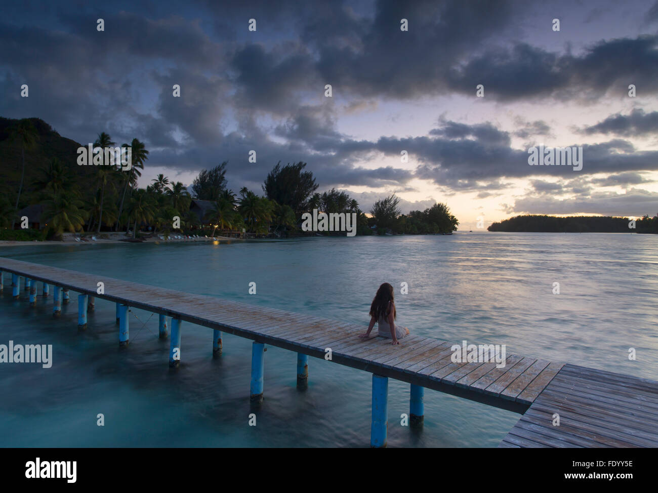 Woman sitting on jetty at sunset, Hauru Point, Mo'orea, Society Islands ...