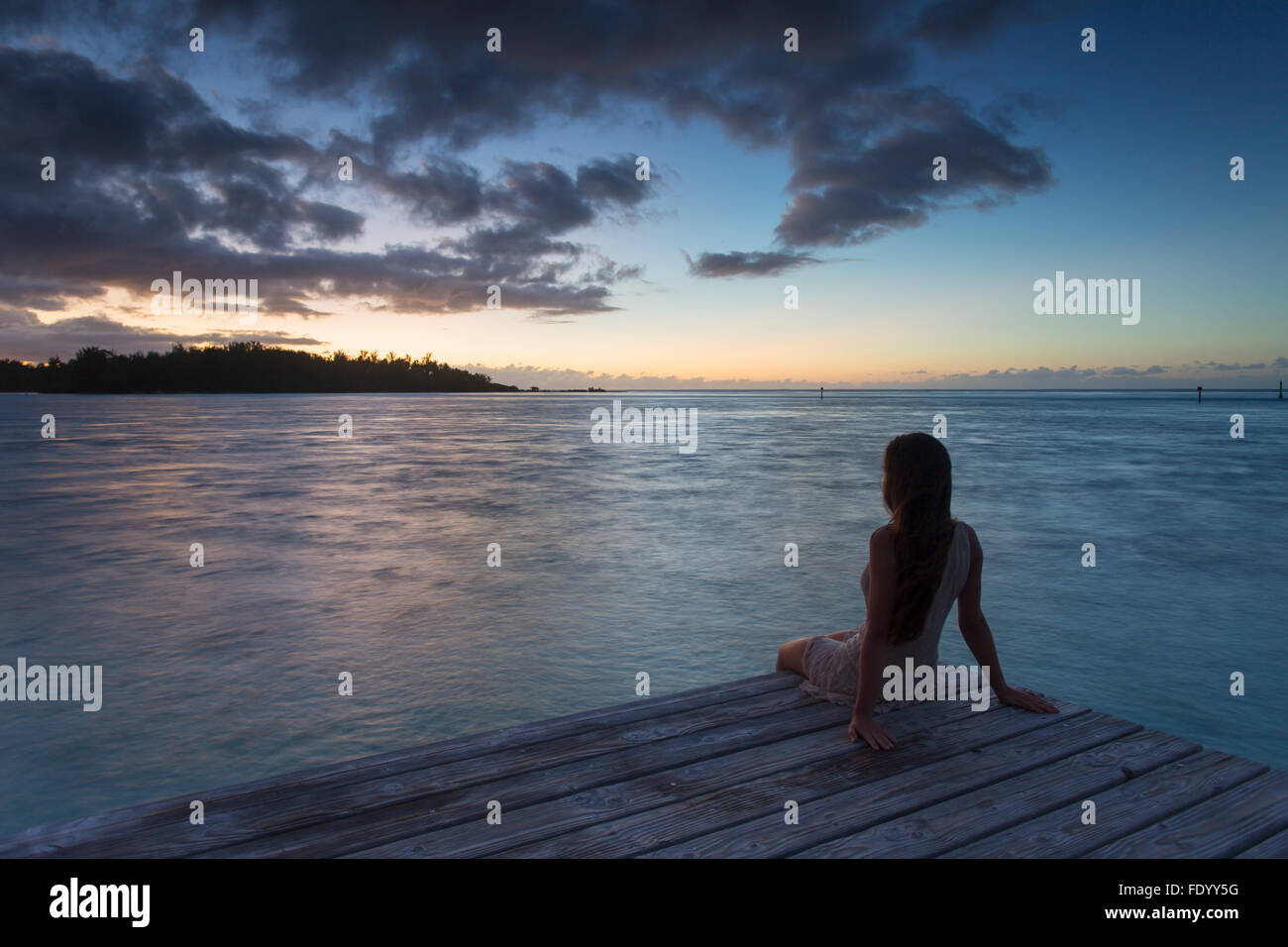 Woman sitting on jetty at sunset, Hauru Point, Mo'orea, Society Islands ...