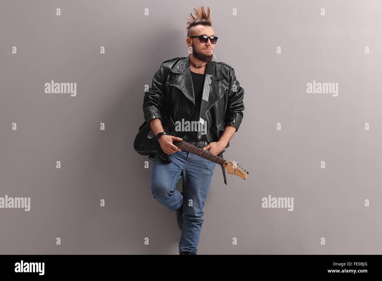 Young punk rock guitarist in black leather jacket holding a guitar and ...