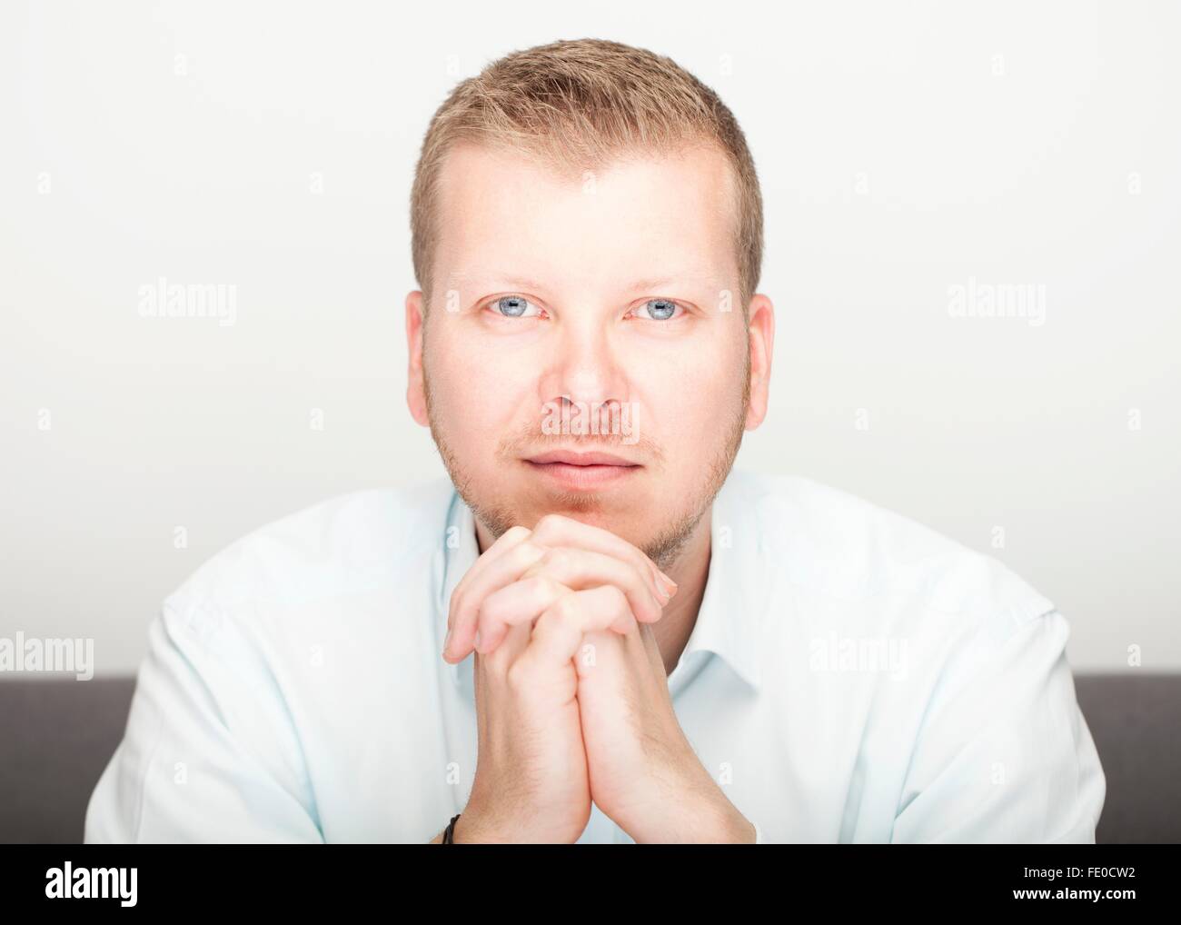Young blue eyed man sitting with his chin resting on his hands looking ...