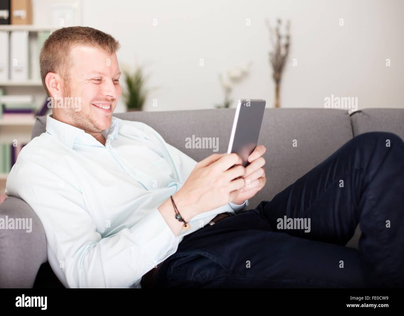 Thoughtful man reading his tablet computer as he relaxes on a couch ...