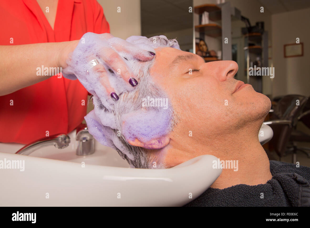 Close up of face of man is getting a hairwash by a hairdresser, with ...