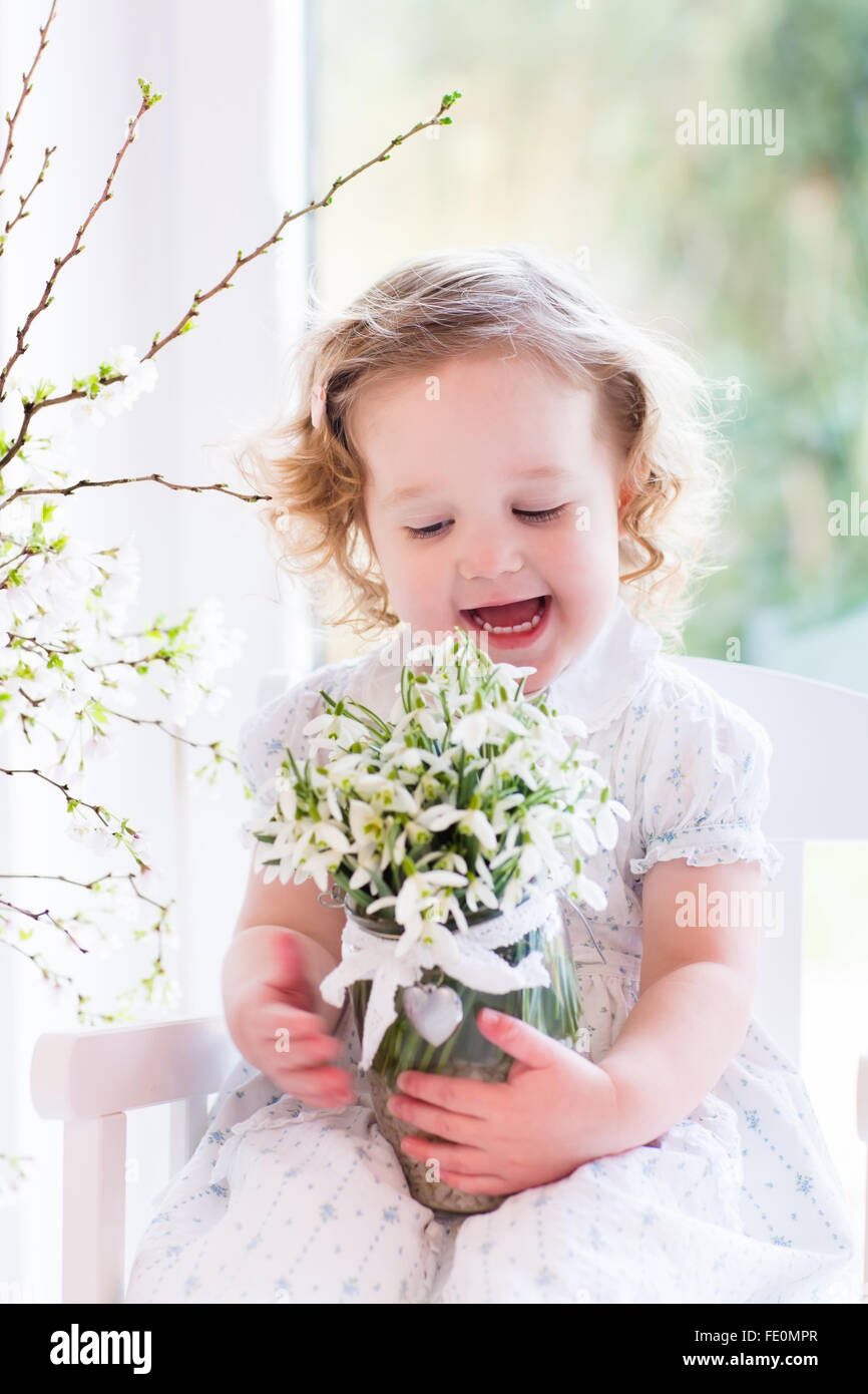 Little girl playing with first spring flowers at home. Child watering ...