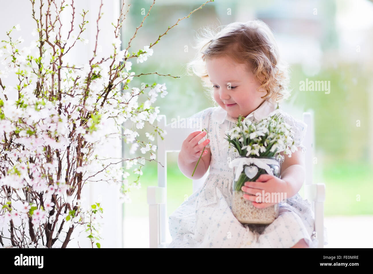 Little girl playing with first spring flowers at home. Child watering ...