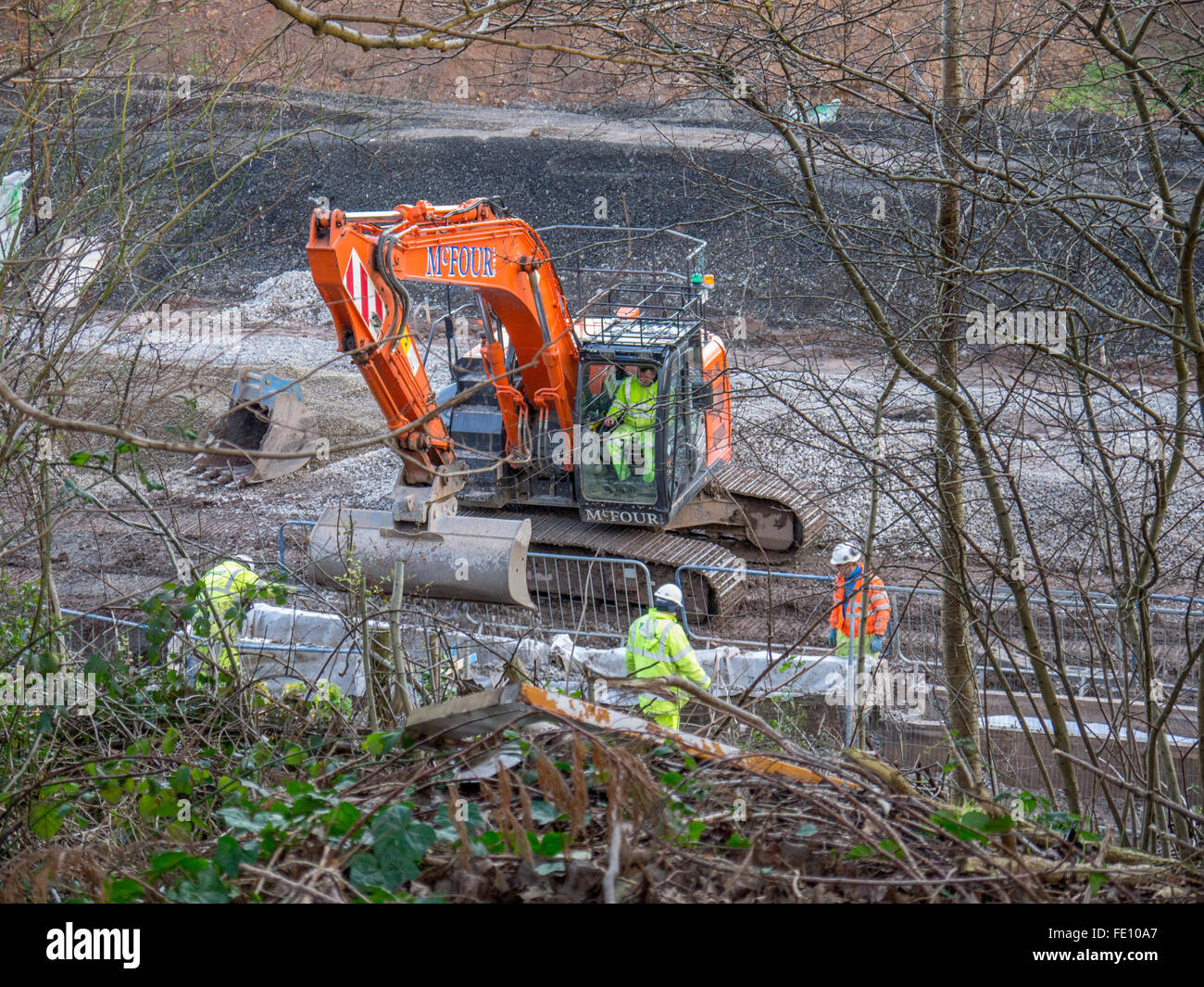 Digger unloading stones with the guidance from 3 workers in safety gear ...