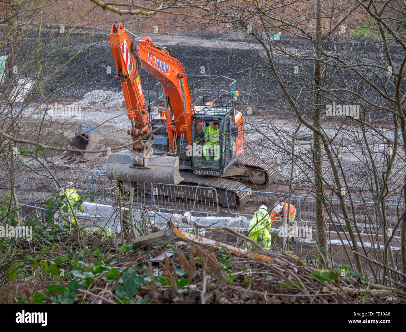 Digger unloading stones with the guidance from 3 workers in safety gear ...