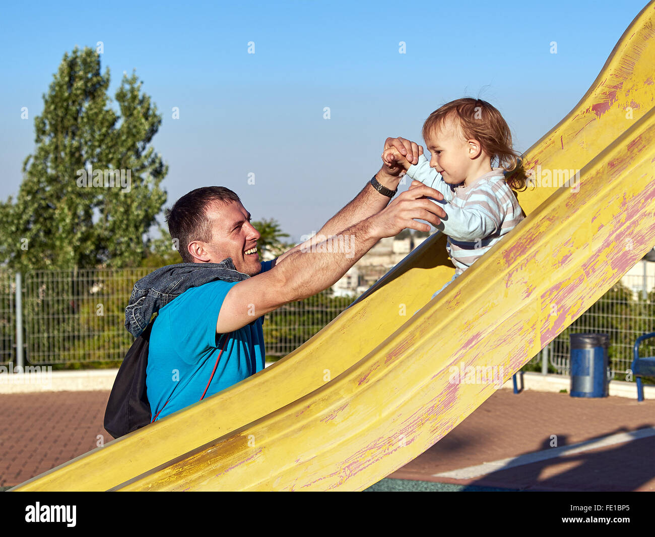Father and cute baby child little boy playing on a slide in playground ...