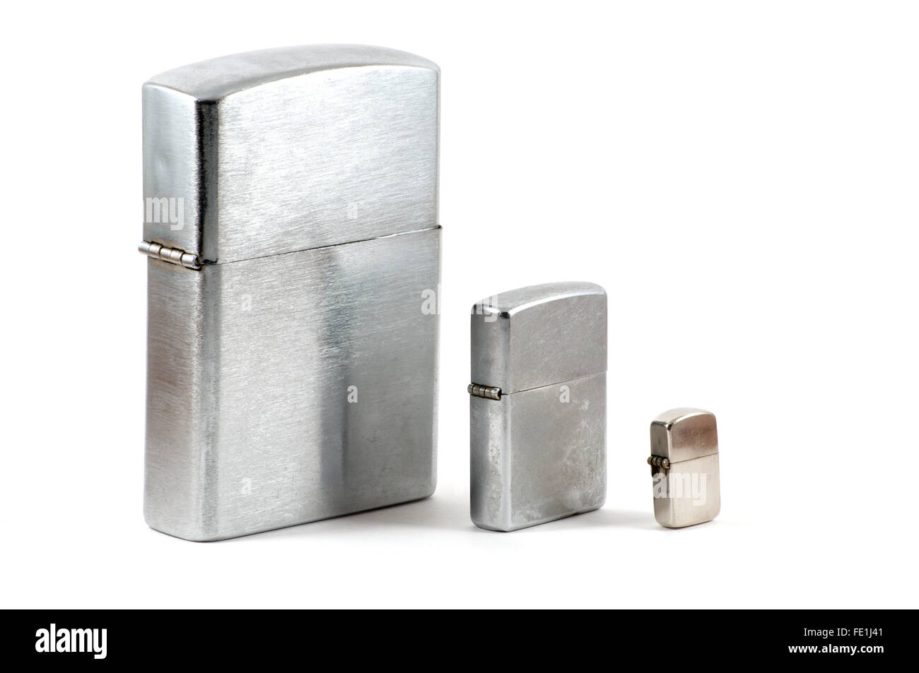 Three different sizes of metallic lighters with cap closed over white ...