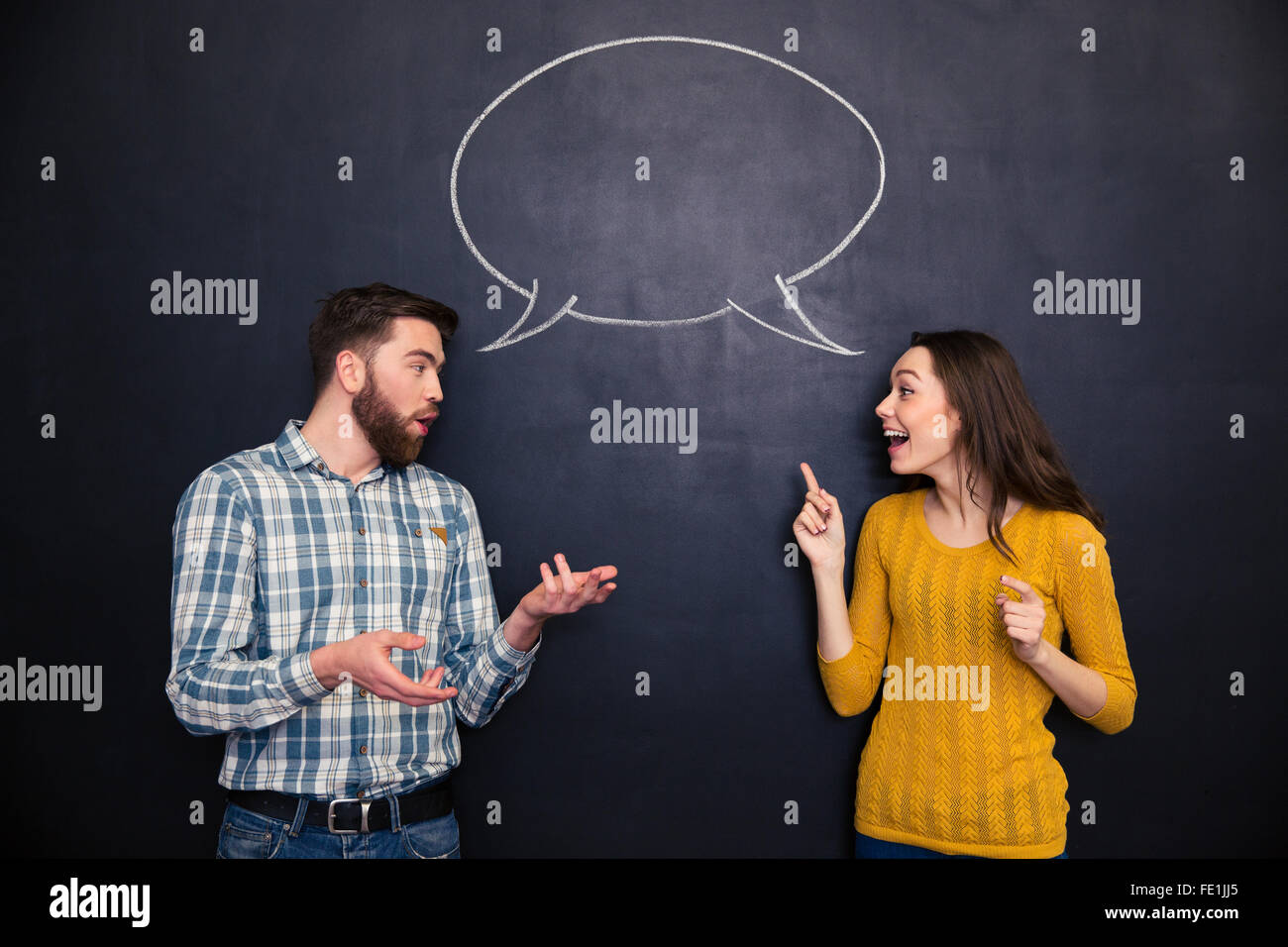 Beautiful happy couple standing and talking over blackboard background ...