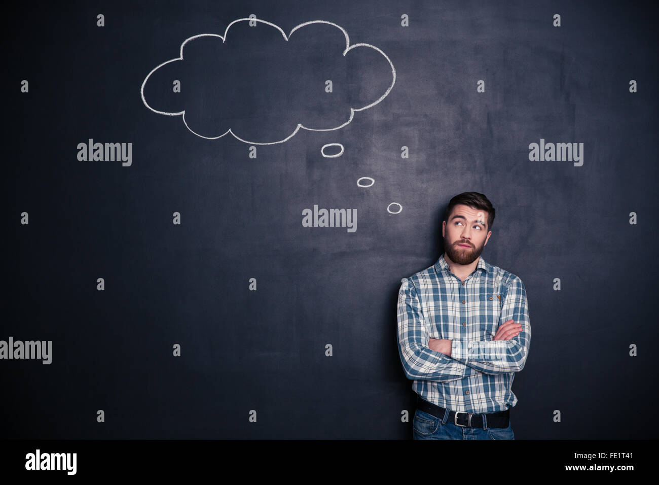 Pensive man standing with arms folded over black background and looking ...