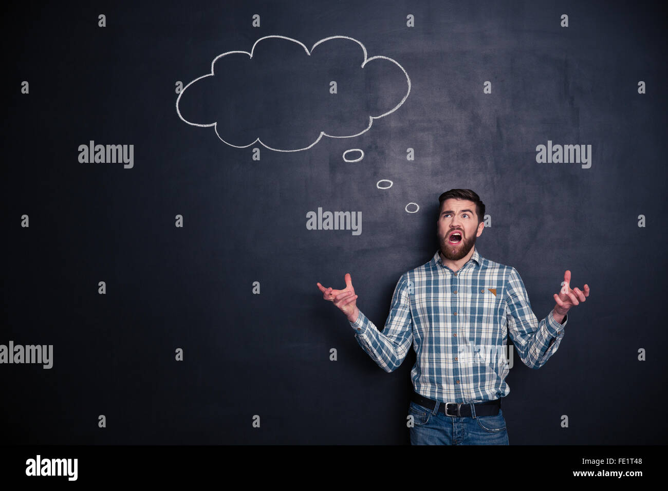 Confused angry bearded man shouting and standing on blackboard ...