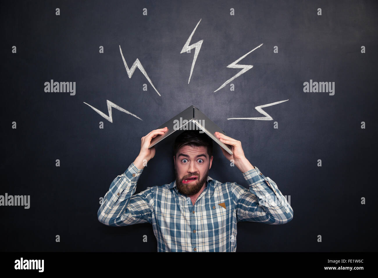 Funny shocked young man holding laptop above his head immitating roof ...