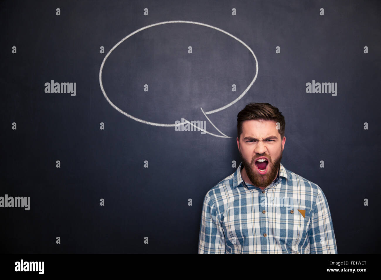 Portrait of angry young man with beard standing and shouting over ...