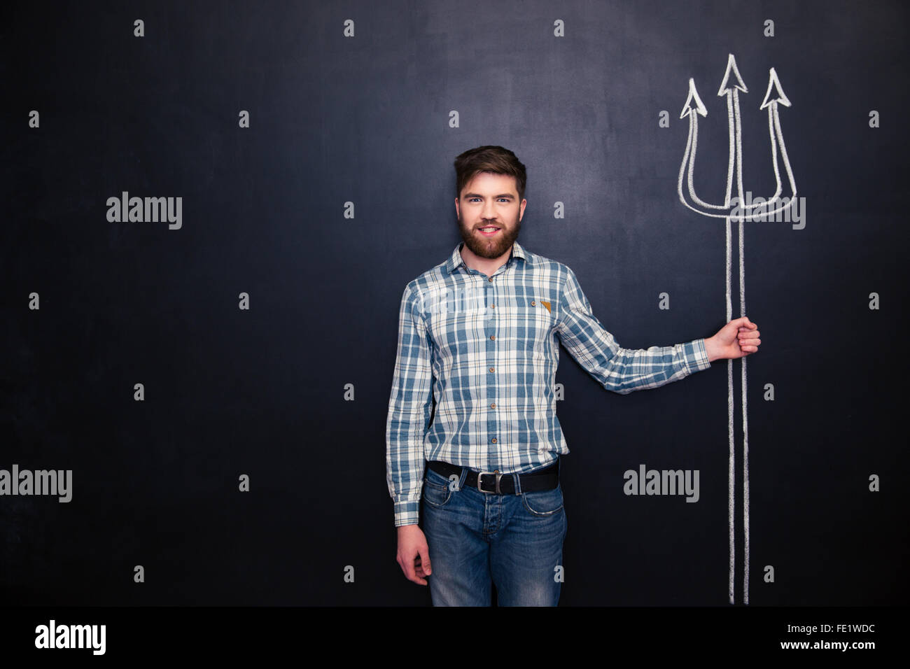 Smiling bearded young man standing and holding drawing trident over ...