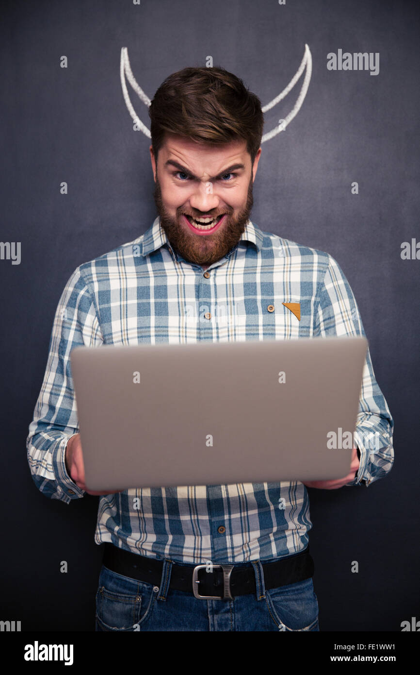 Funny bearded young man using laptop and standing over blackboard ...
