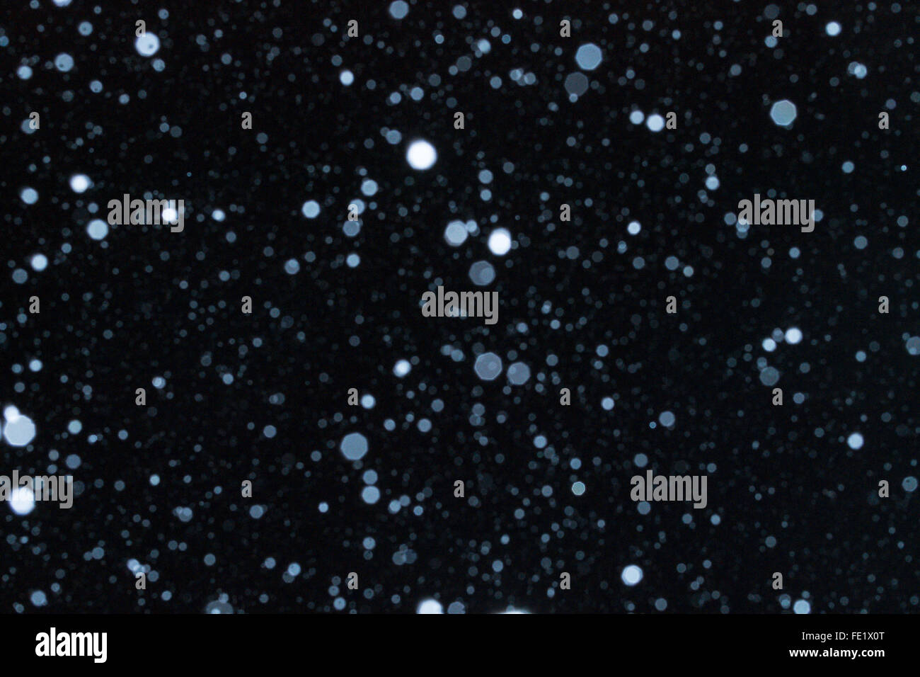 Flakes of natural snow falling at night set against a black background ...